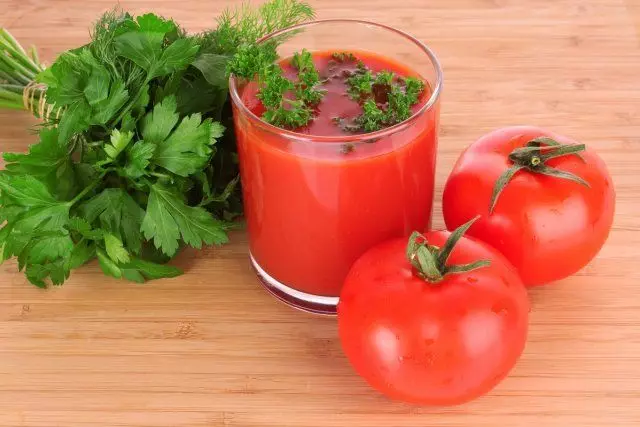 Salamin ng sariwang tomato juice at mga kamatis sa paligid ng salamin sa mesa