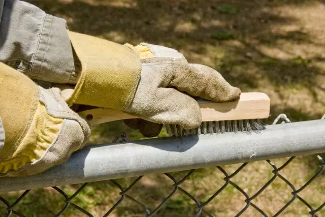 Arbeidstaker med hansker på wire børsting et kjede link gjerde