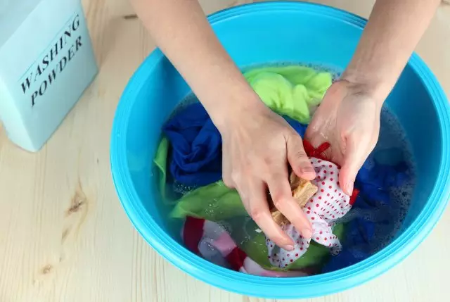 Hand washing in plastic bowl on wooden table close-up