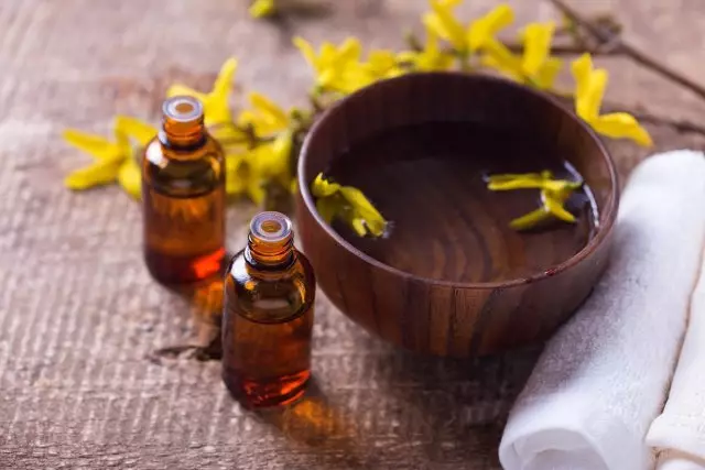 Spa setting. Essential aroma oil, water in bowl, towels, yellow flowers on aged wooden background. Selective focus.