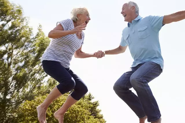 Senior Couple Bouncing On Trampoline In Garden